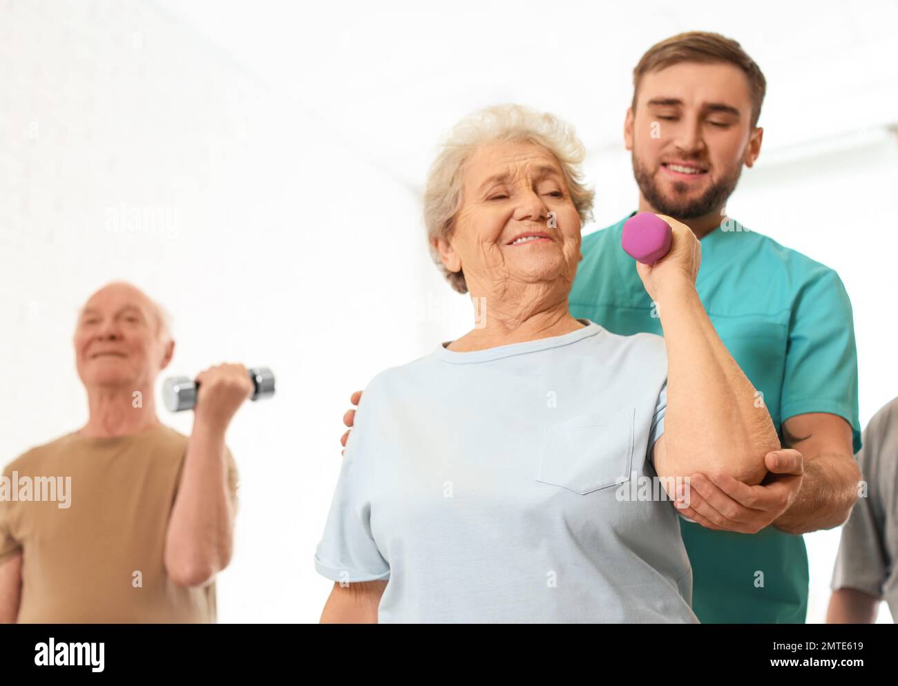 Care worker helping elderly woman to do exercise with dumbbell in hospital gym Stock Photo - Alamy