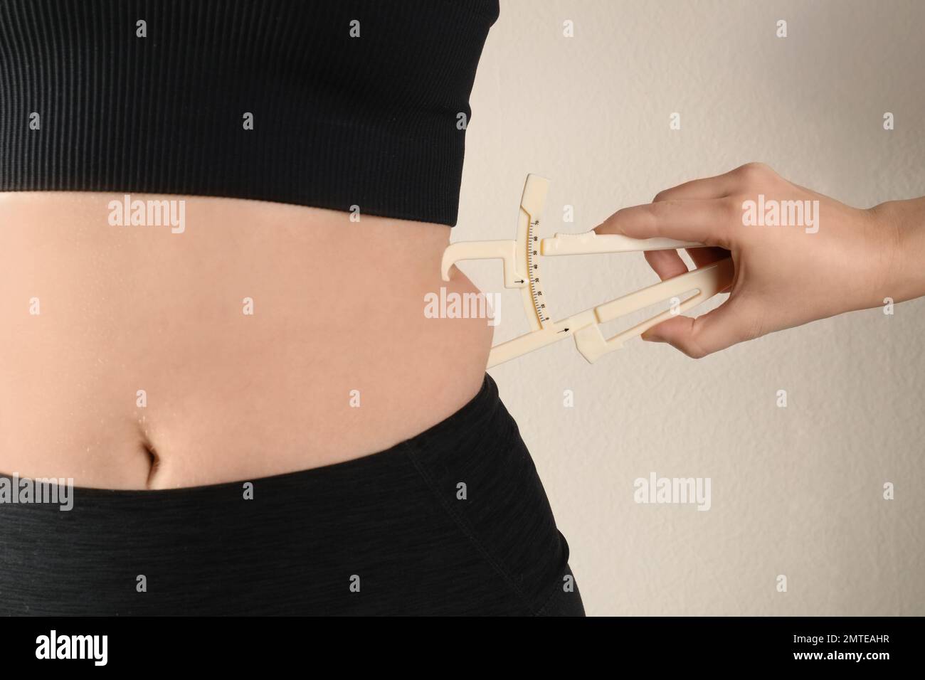 Nutritionist measuring woman's body fat layer with caliper on beige ...