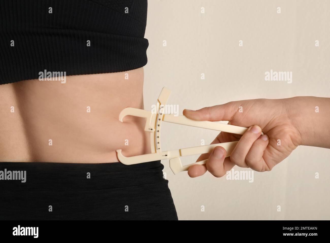 Nutritionist measuring woman's body fat layer with caliper on beige ...