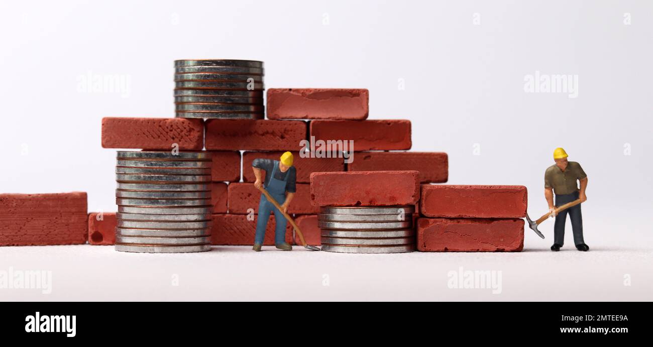 Miniature workers building bricks. Business concept with coins and ...