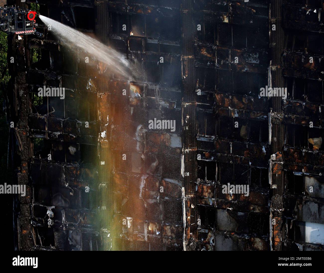The sun creates a rainbow effect as firefighters work at the scene of a ...