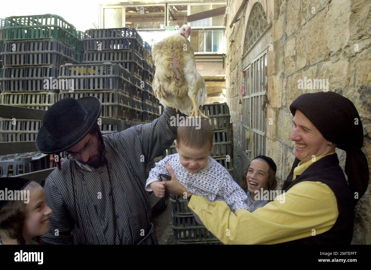 An ultra-Orthodox Jewish man holds a chicken above his child held by ...