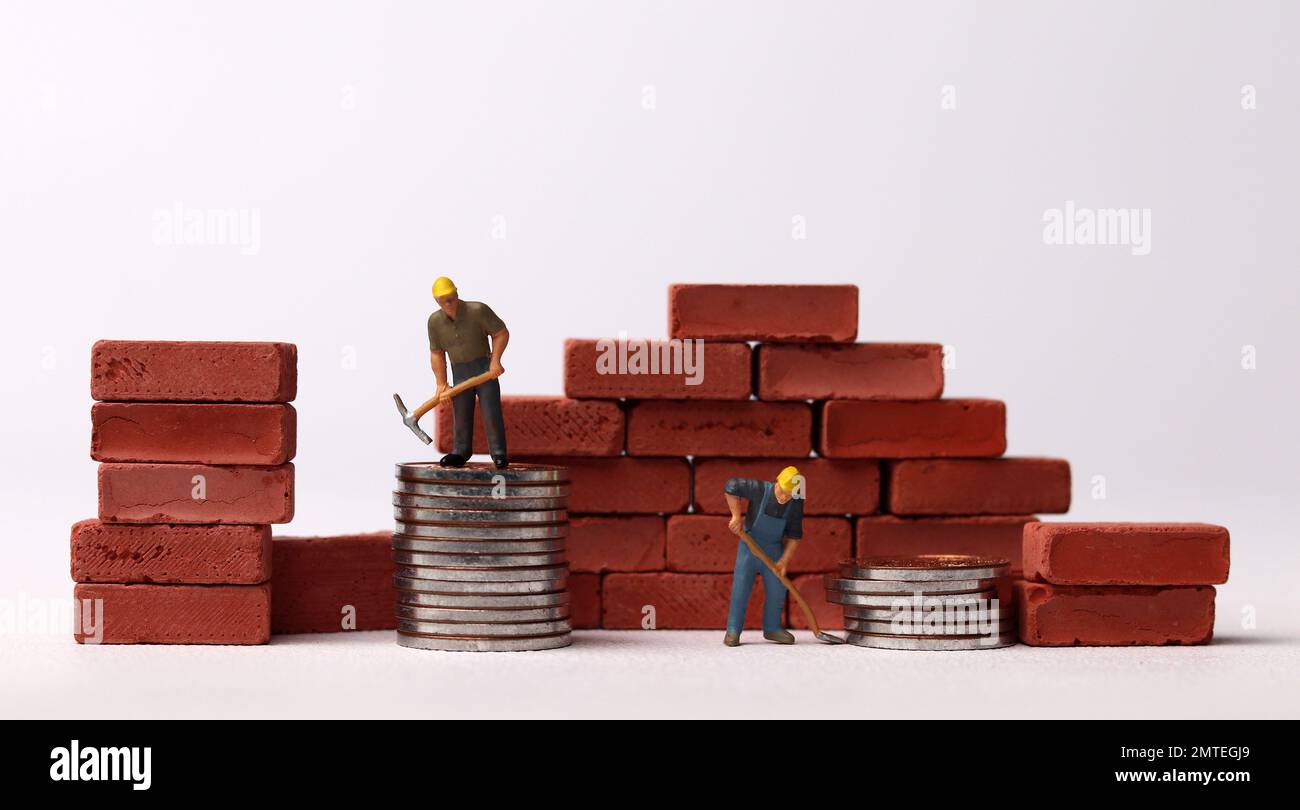 Miniature workers building bricks. Business concept with coins and ...