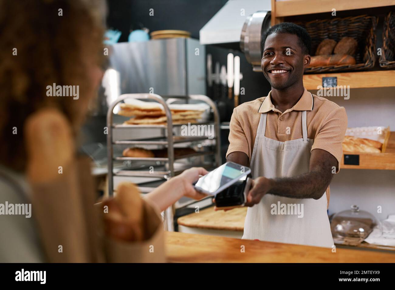 Smiling friendly cashier desk worker accepting contactless payment ...