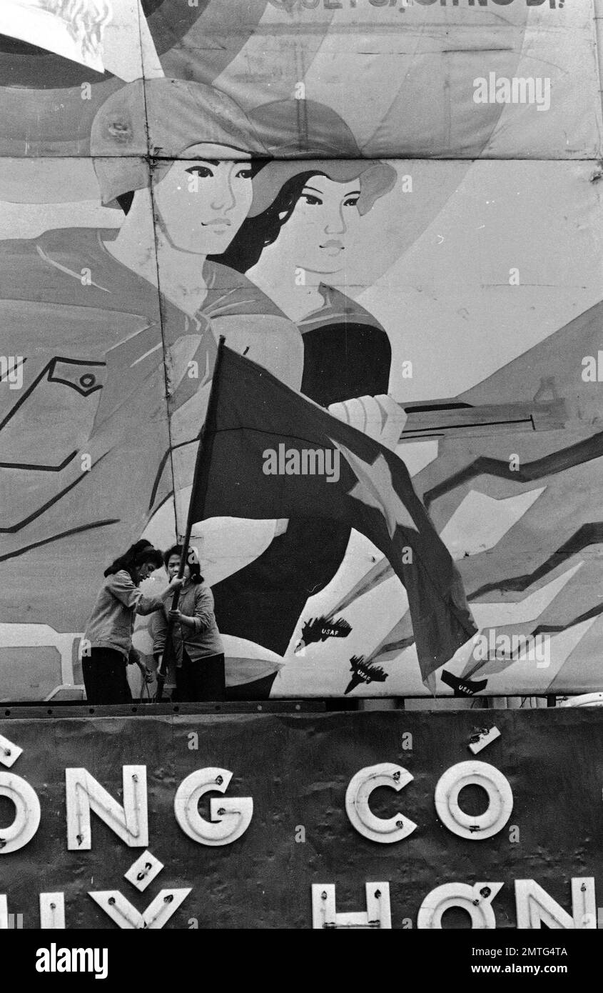 Two North Vietnamese women hoist the national flag on top of a public ...
