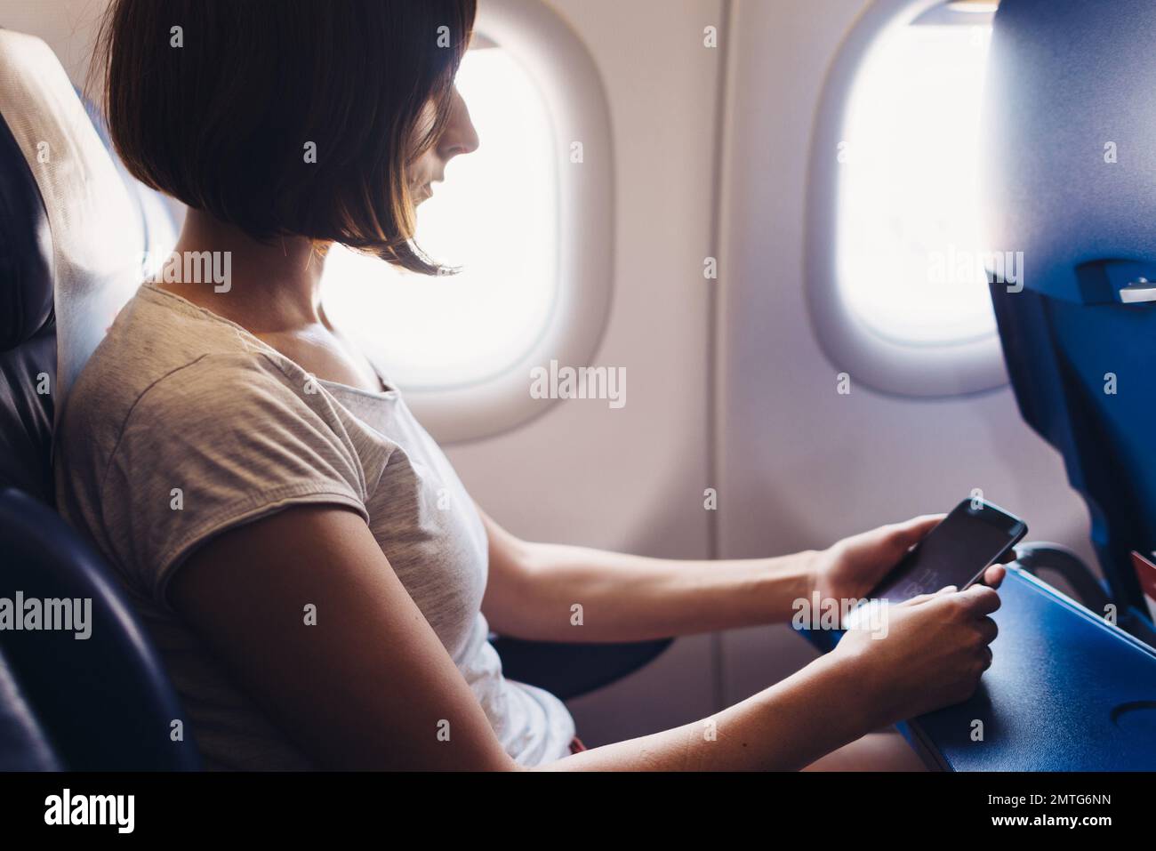 Young woman on a plane with a smartphone in her hands Stock Photo - Alamy