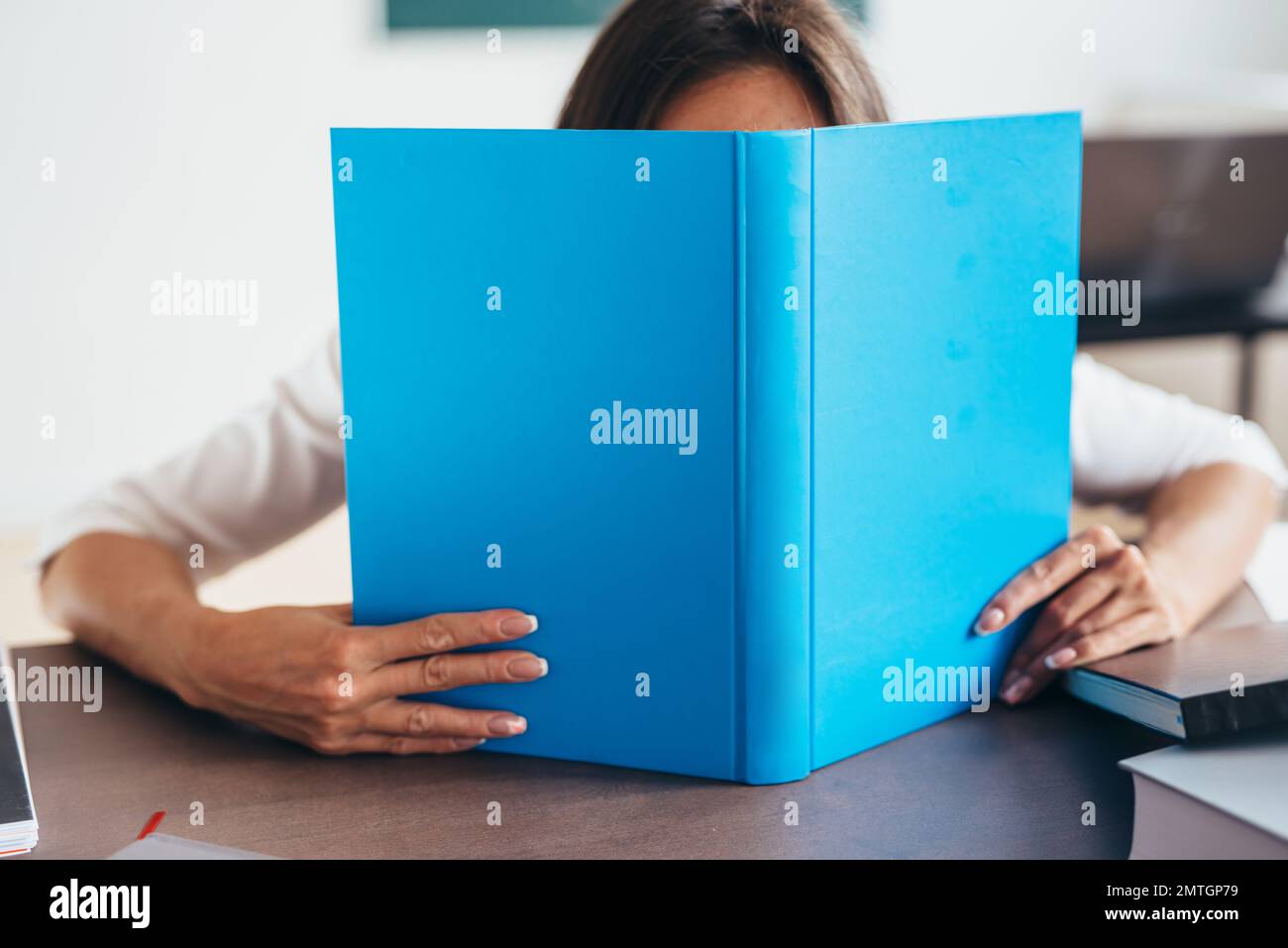 Female student hiding behind an open book Stock Photo - Alamy