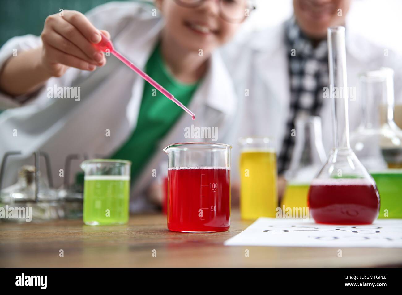 Teacher with pupil making experiment at table in chemistry class, focus ...