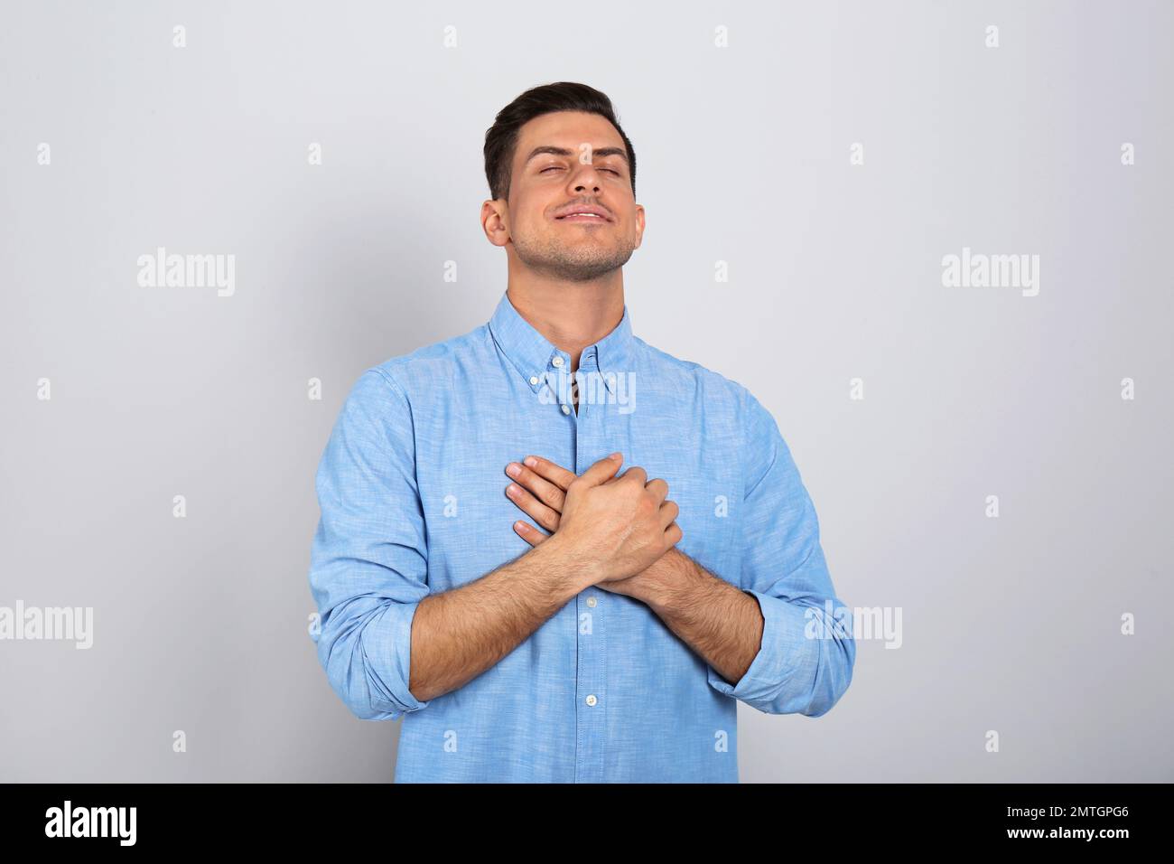 Handsome grateful man with hands on chest against light grey background ...
