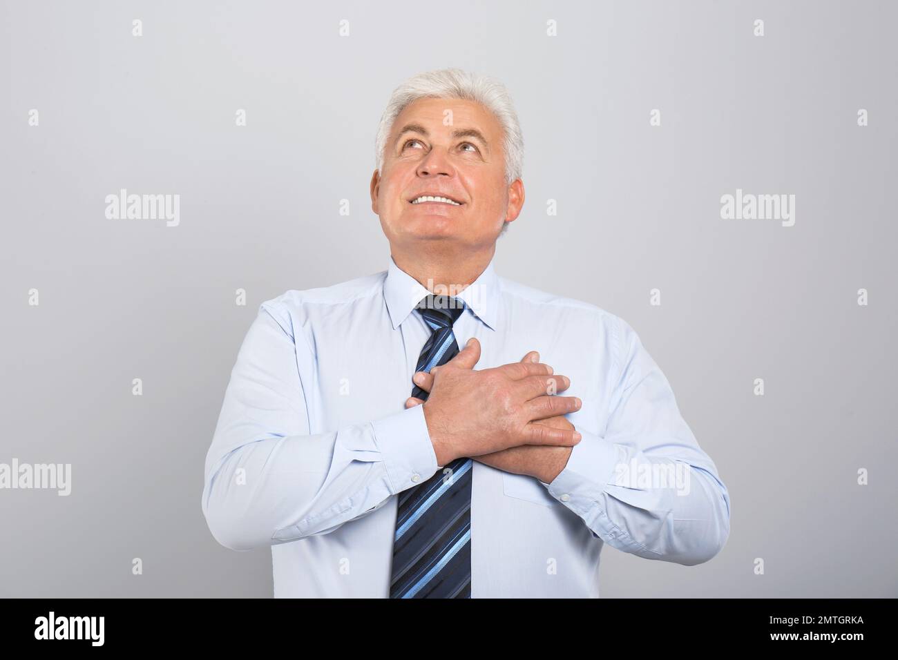 Grateful senior man with hands on chest against light grey background ...