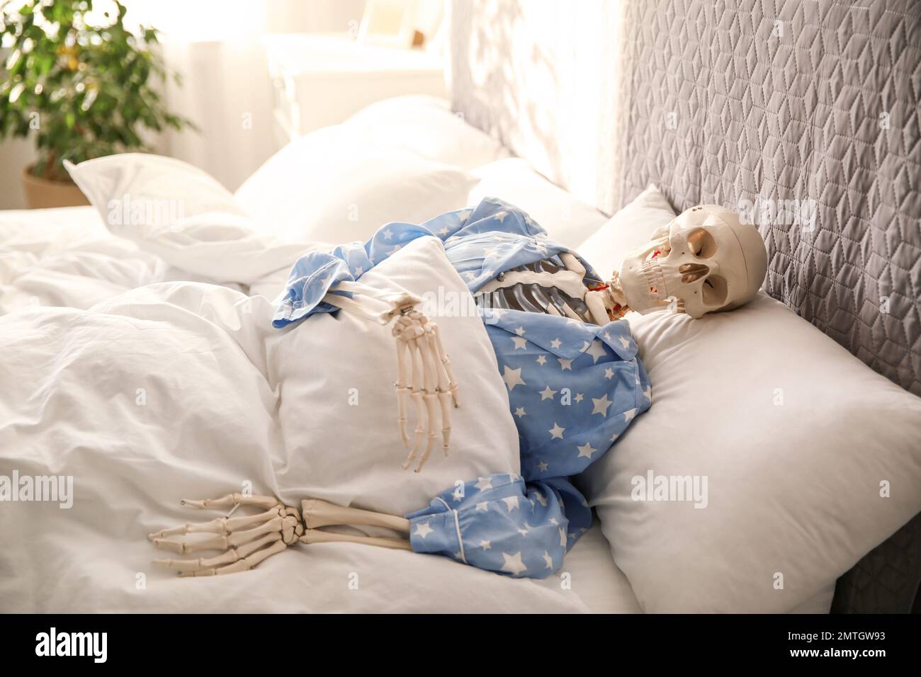 Human skeleton in pajamas lying on bed indoors Stock Photo - Alamy