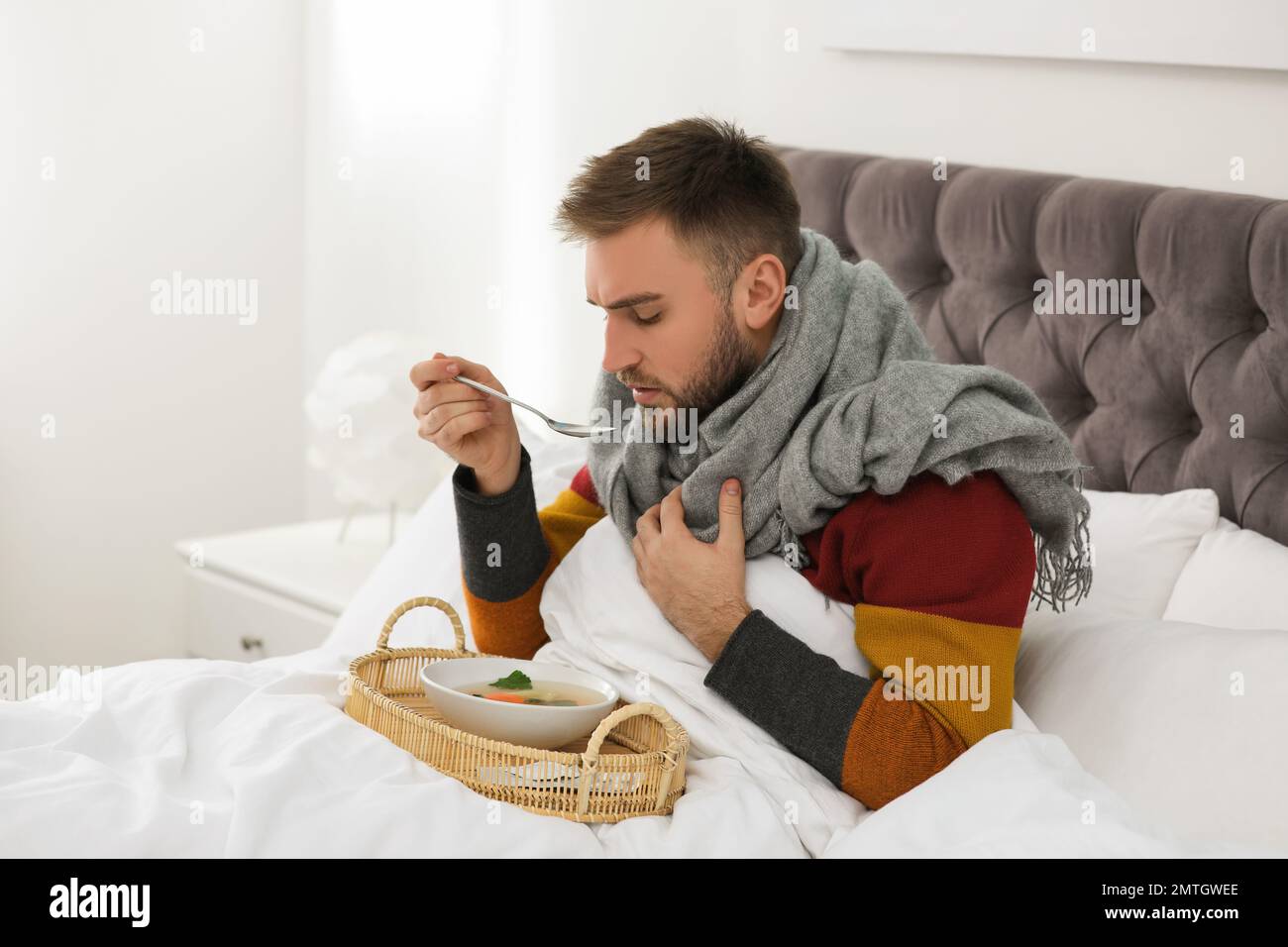 Sick young man with bowl of tasty soup in bed at home Stock Photo - Alamy