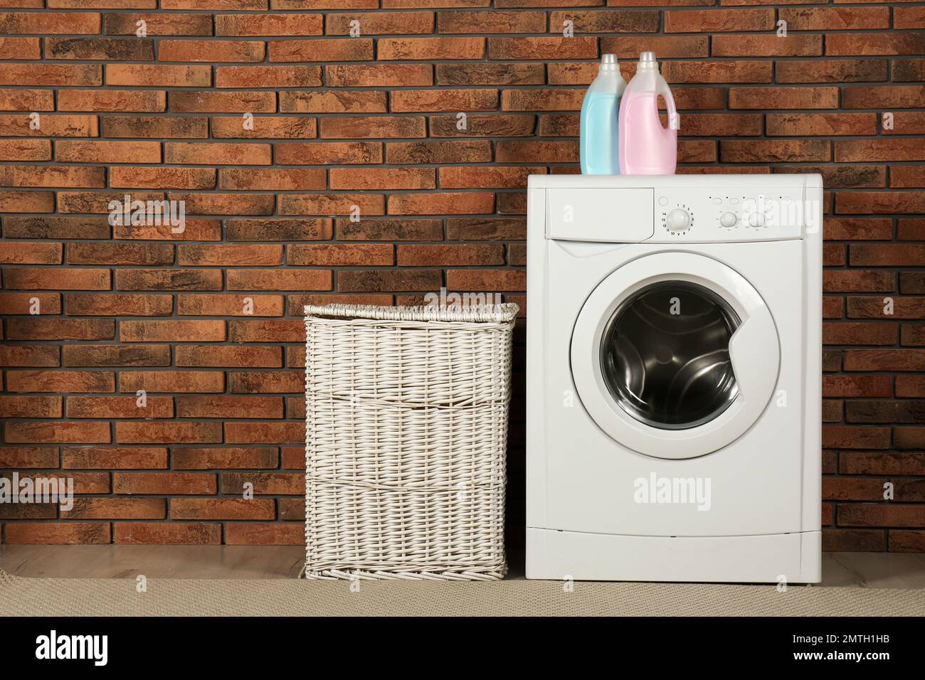 Modern washing machine with detergent and laundry basket near brick ...