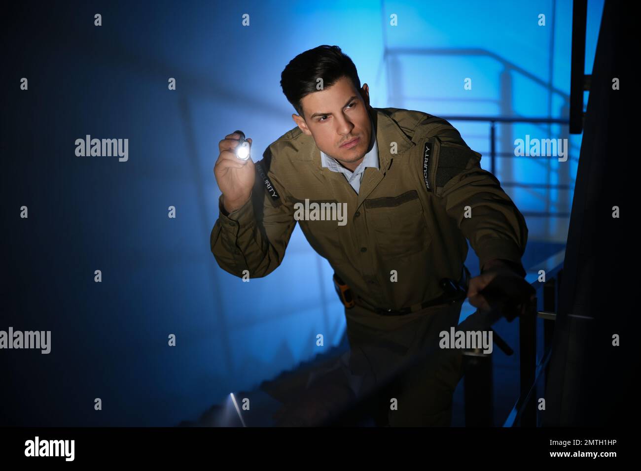 Professional security guard with flashlight on stairs in dark room ...