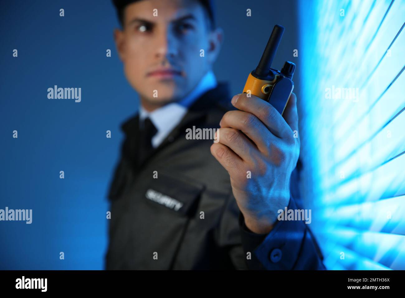 Professional security guard with portable radio set near window in dark ...