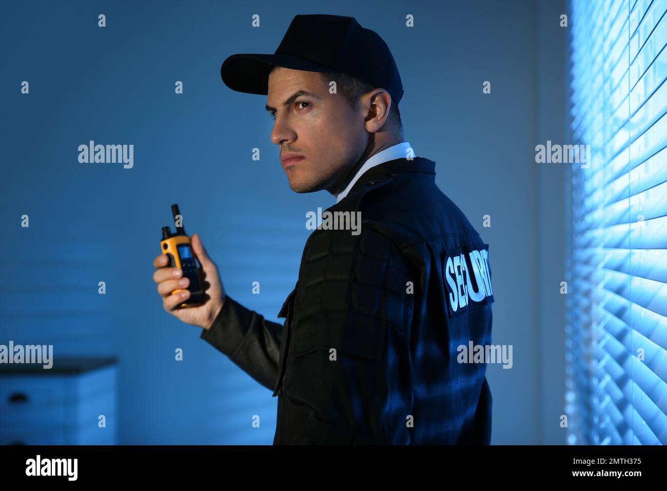 Professional security guard with portable radio set near window in dark ...