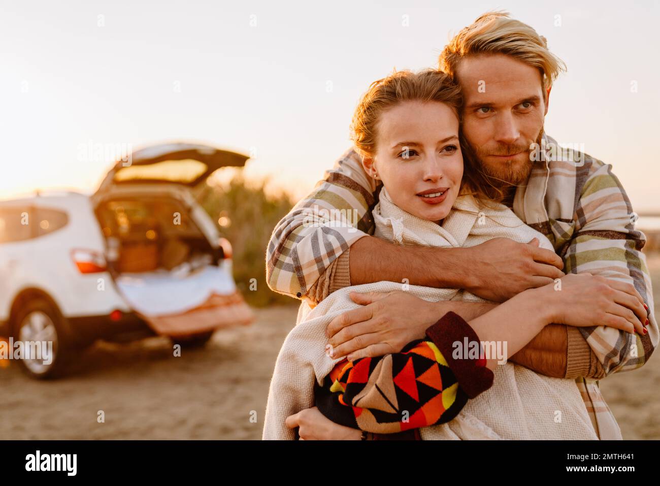 Happy young white couple hugging while walking by seashore on sunny day ...
