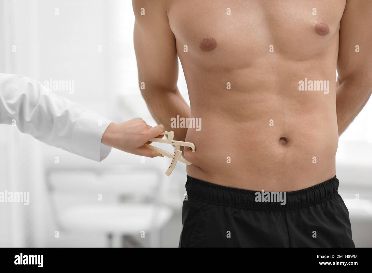 Nutritionist measuring man's body fat layer with caliper on blurred ...