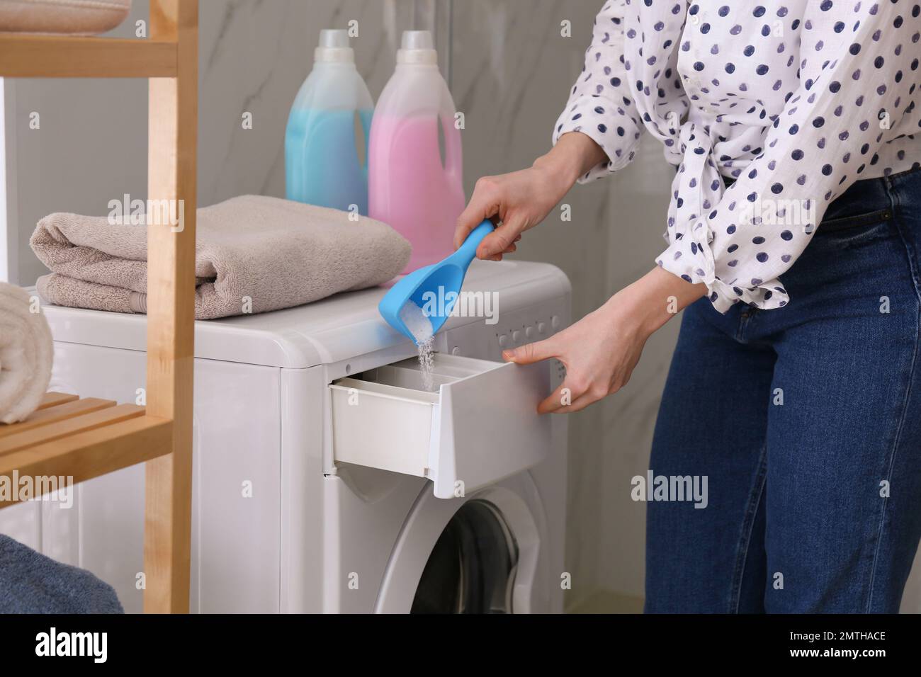 Woman pouring laundry detergent into washing machine drawer in bathroom ...