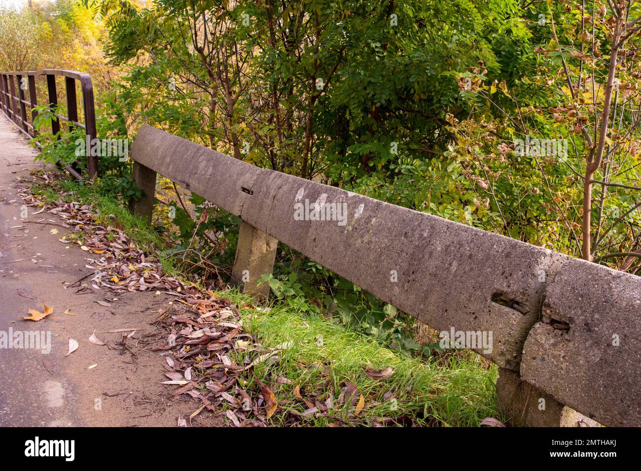 A concrete railing by a deserted and neglected road on a gloomy autumn ...