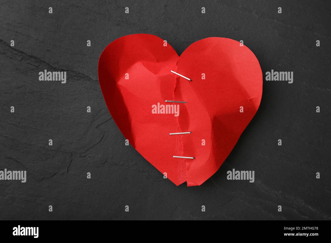 Torn paper heart with staples on black stone background, top view ...