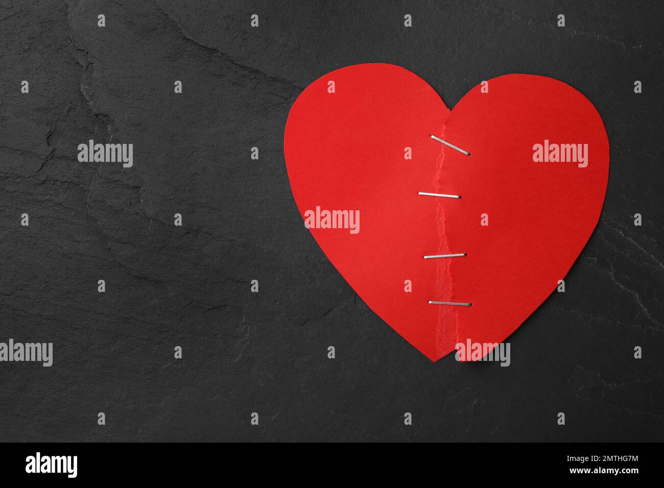 Top view of torn paper heart with staples on black stone background ...