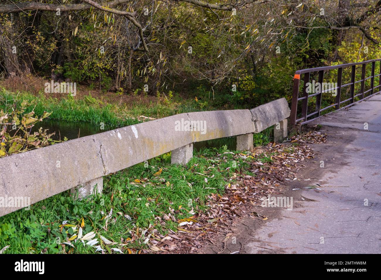 A concrete railing by a deserted and neglected road on a gloomy autumn ...