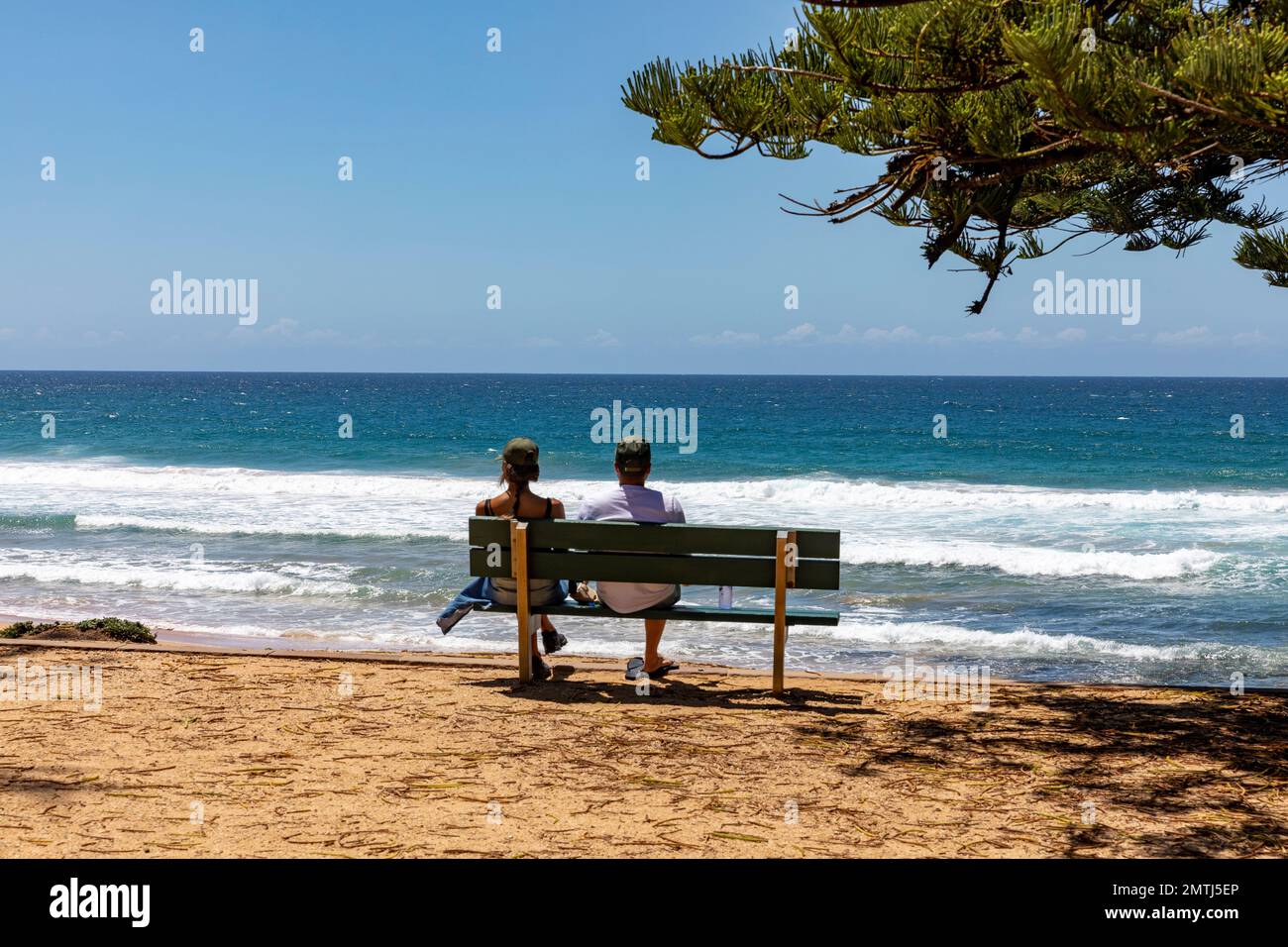 Couple sitting at the beach on a bench staring out to sea ocean, Avalon Beach Sydney east coast ...