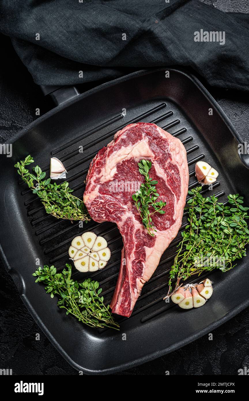 Ready for cooking Raw cowboy or rib eye steak in a grill skillet. Black ...