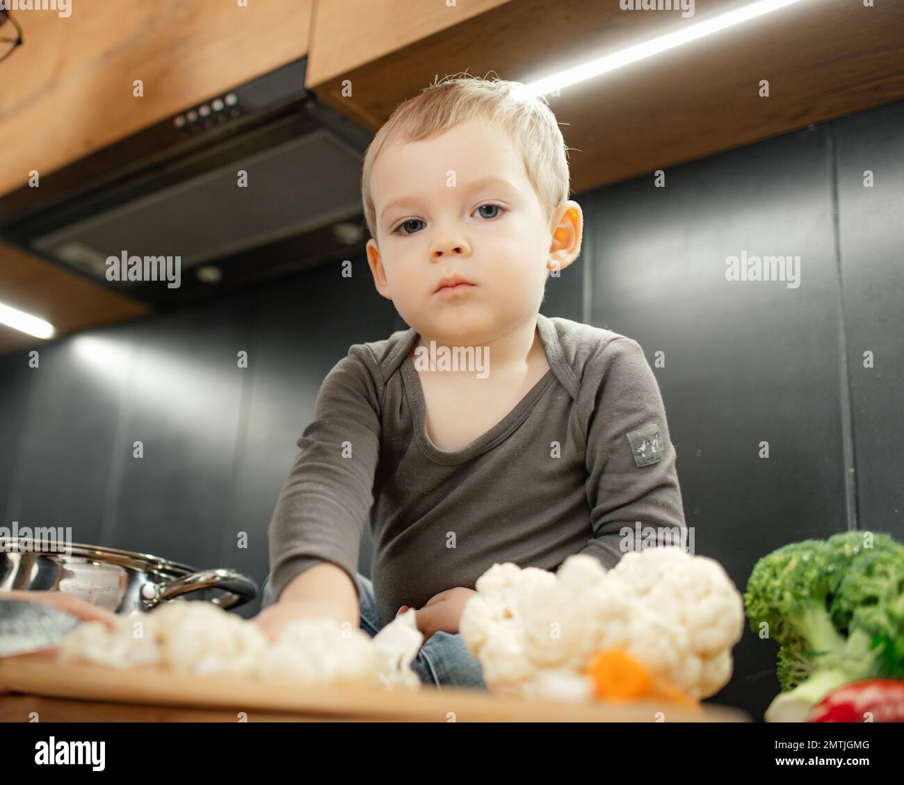 Little child help cooking dinner from below view. Baby son sitting on ...