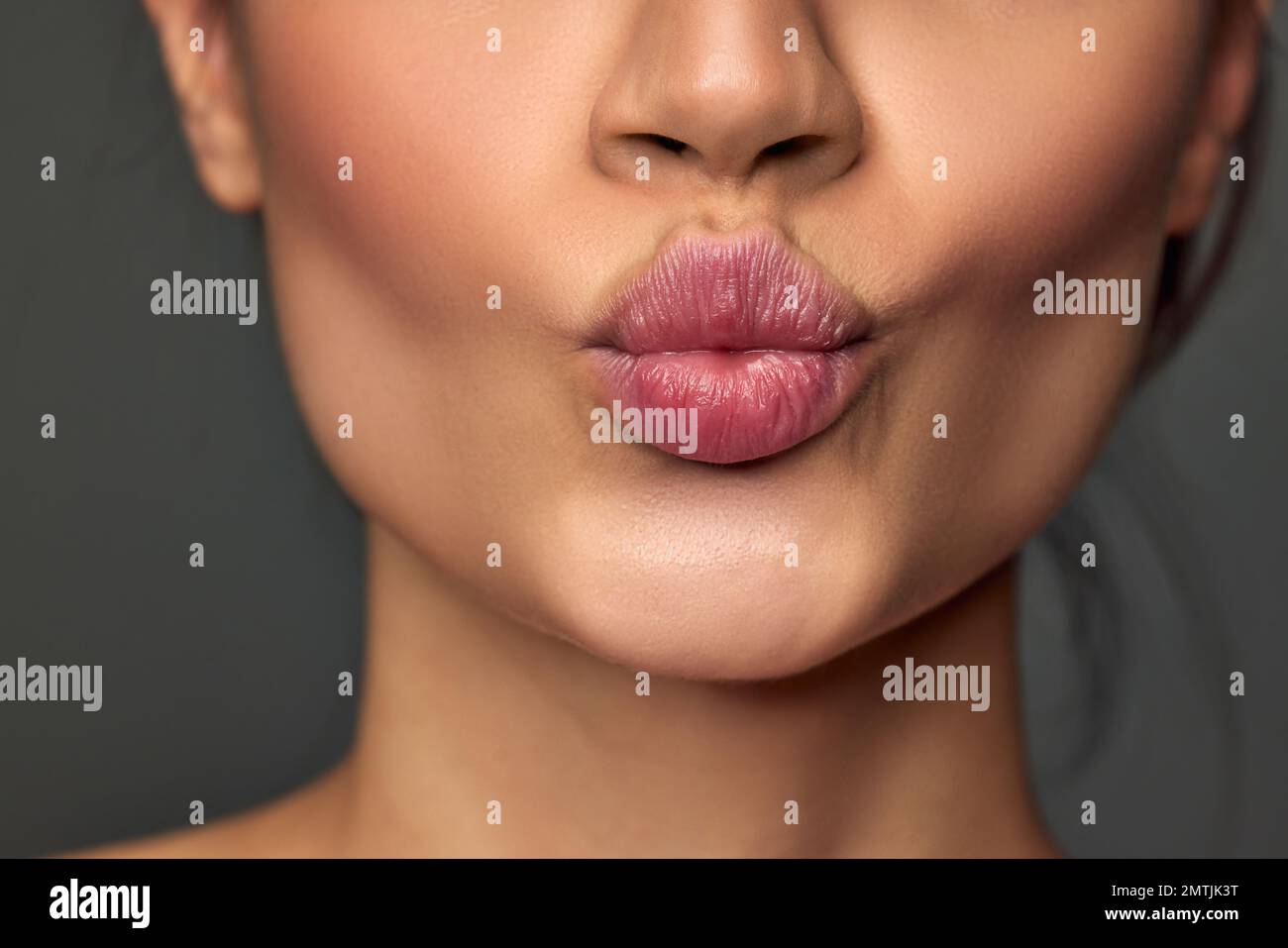Cropped image of female face, lips, nose, chin over grey studio ...