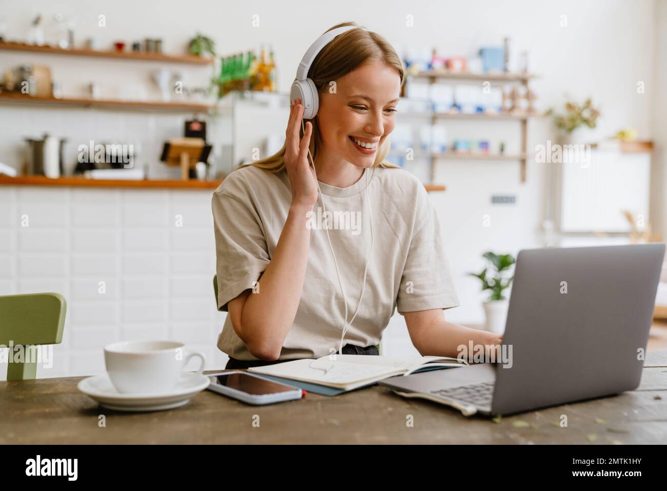 Blonde white woman listening music while working with laptop at cafe ...