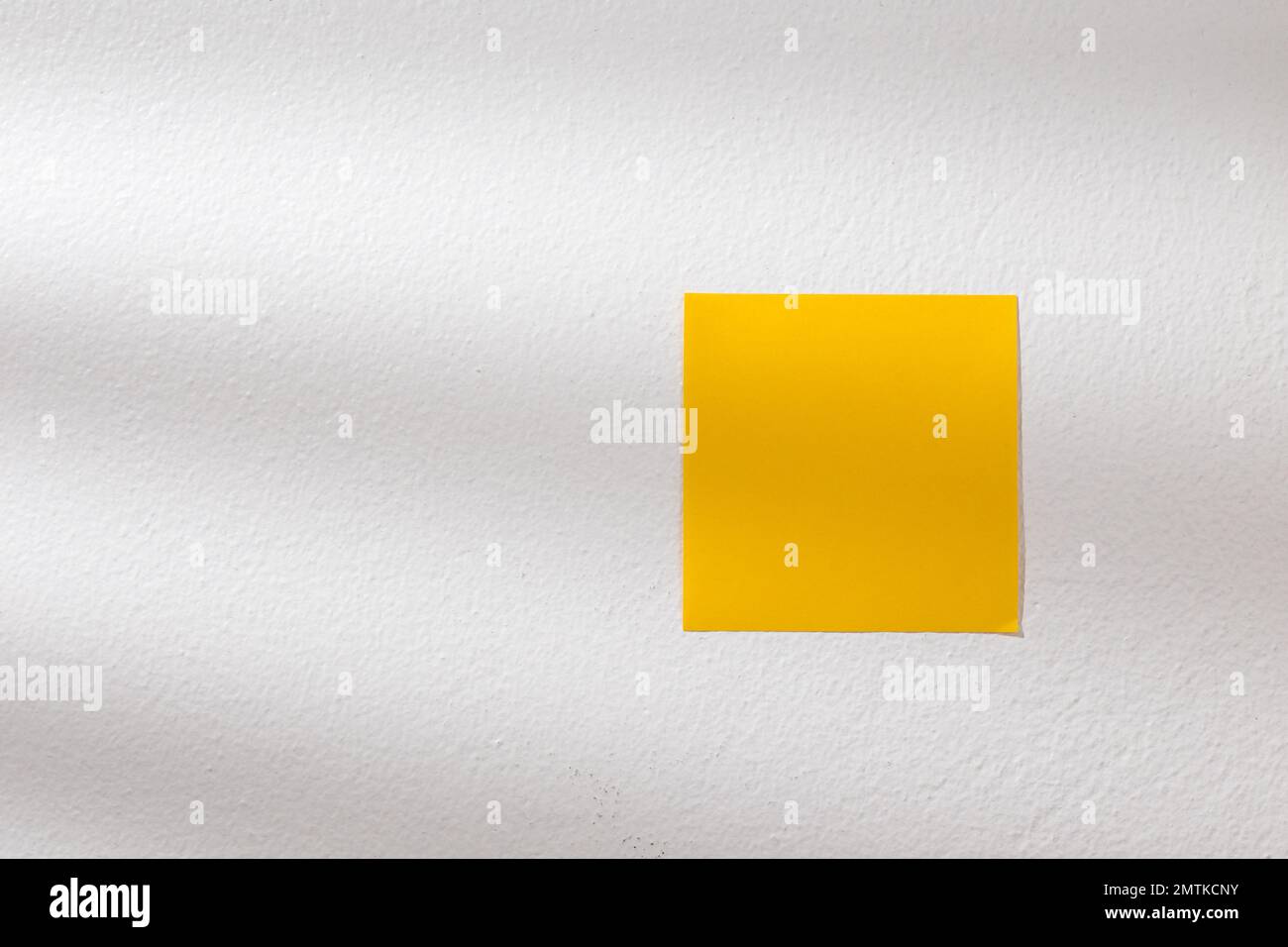 Yellow post it on the white wall Stock Photo - Alamy