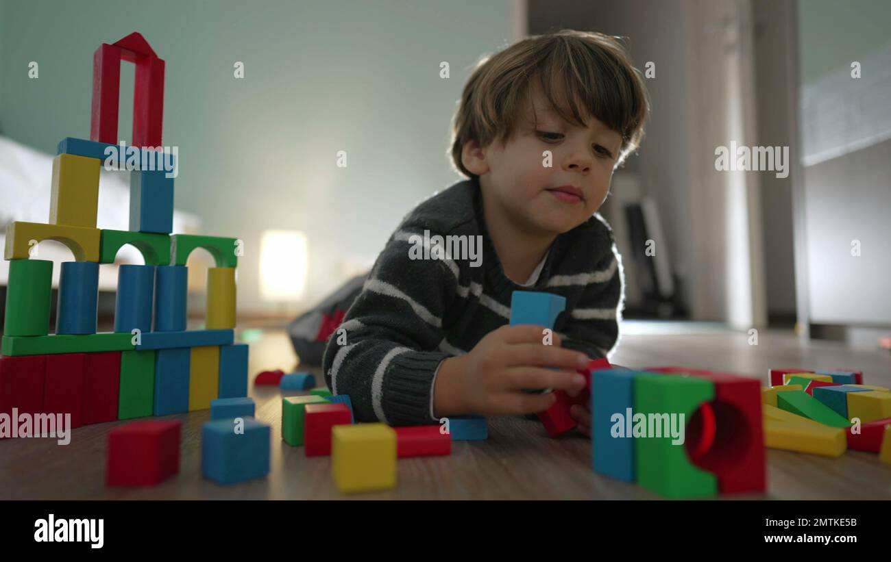 Child laying on floor playing with building blocks. One small boy doing ...