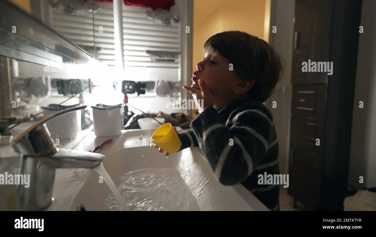 Small boy drinking water and spitting in bathroom sink. Child standing ...