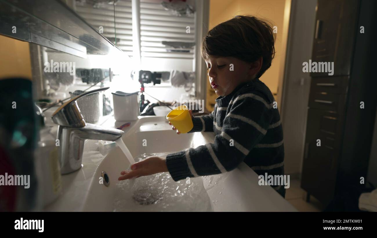 Small boy drinking water and spitting in bathroom sink. Child standing ...