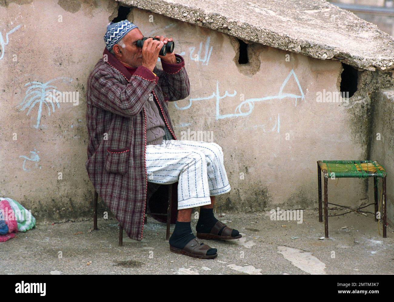 A man looks through binoculars on a rooftop, under curfew and watches ...