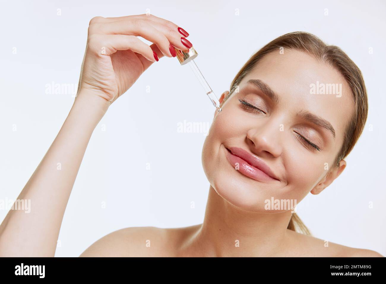 Portrait of young beautiful girl with clear face applying face serum ...