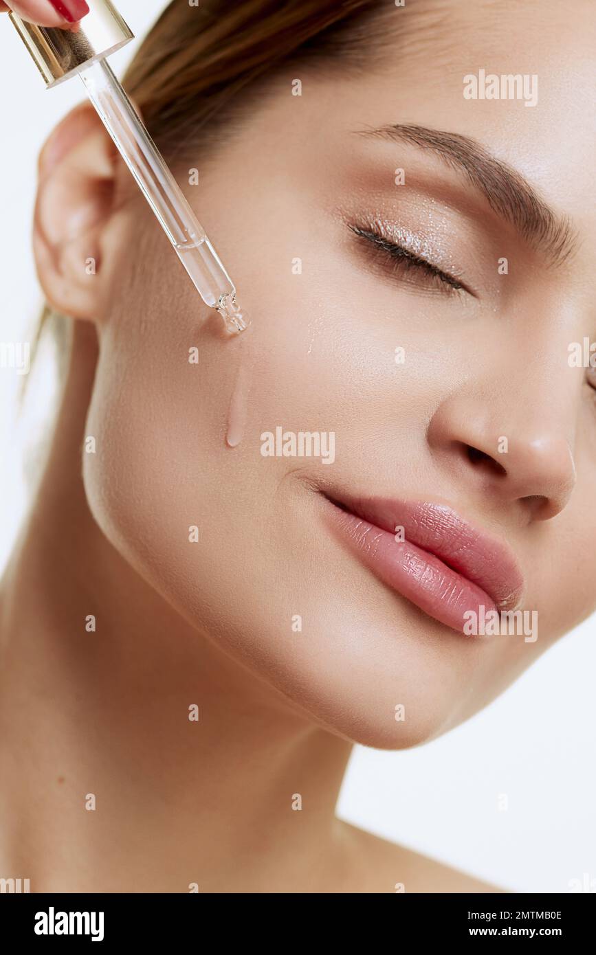 Portrait of young beautiful girl with clear face applying face serum ...