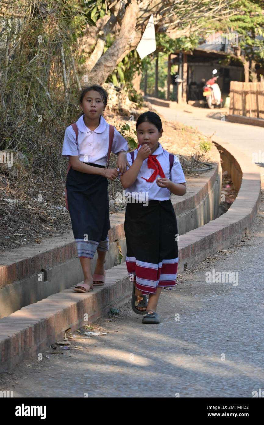 Two little girls in school uniform go back to their home in a rural ...