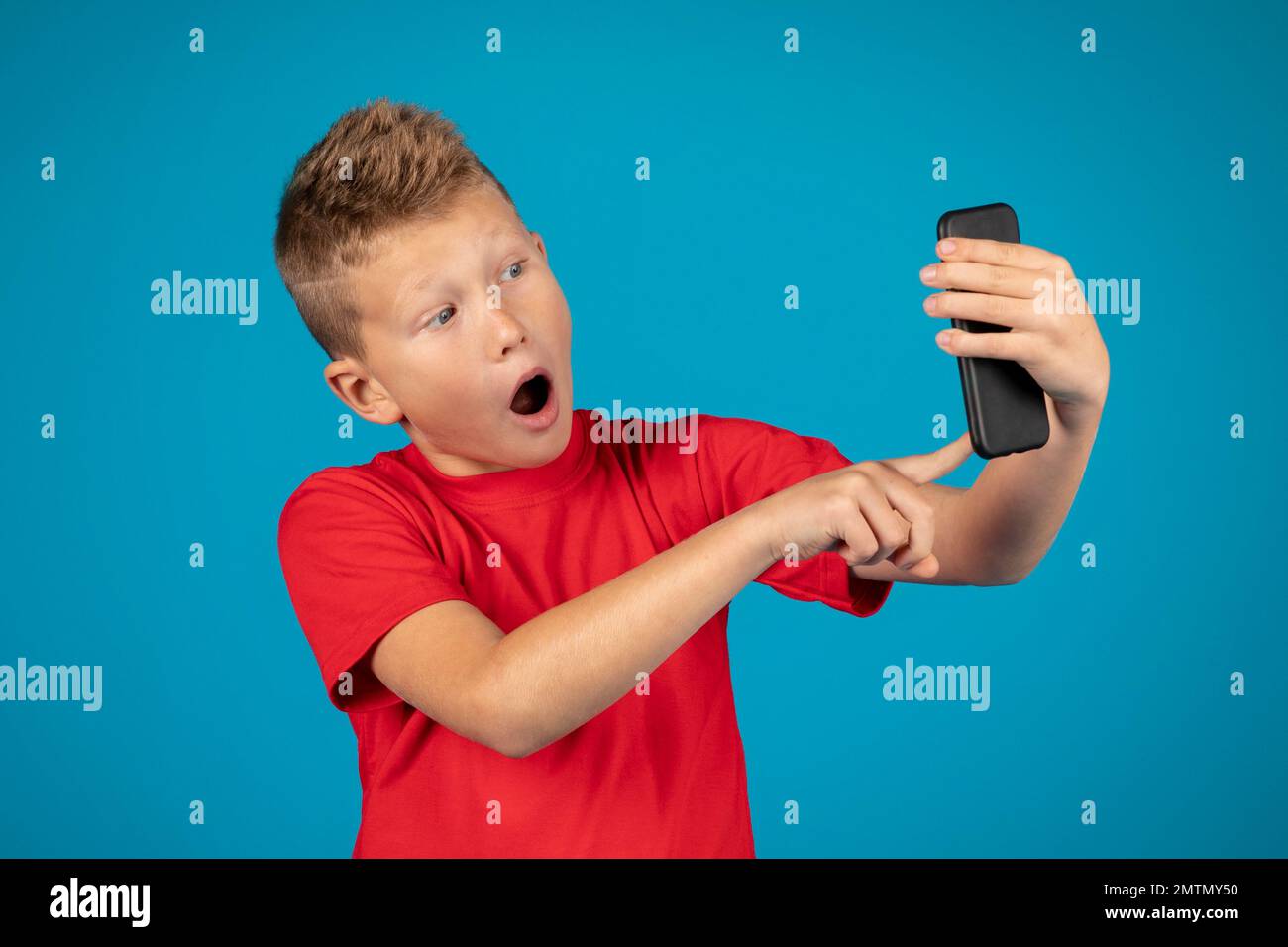 Portrait of scared preteen boy using smartphone and opening mouth in ...