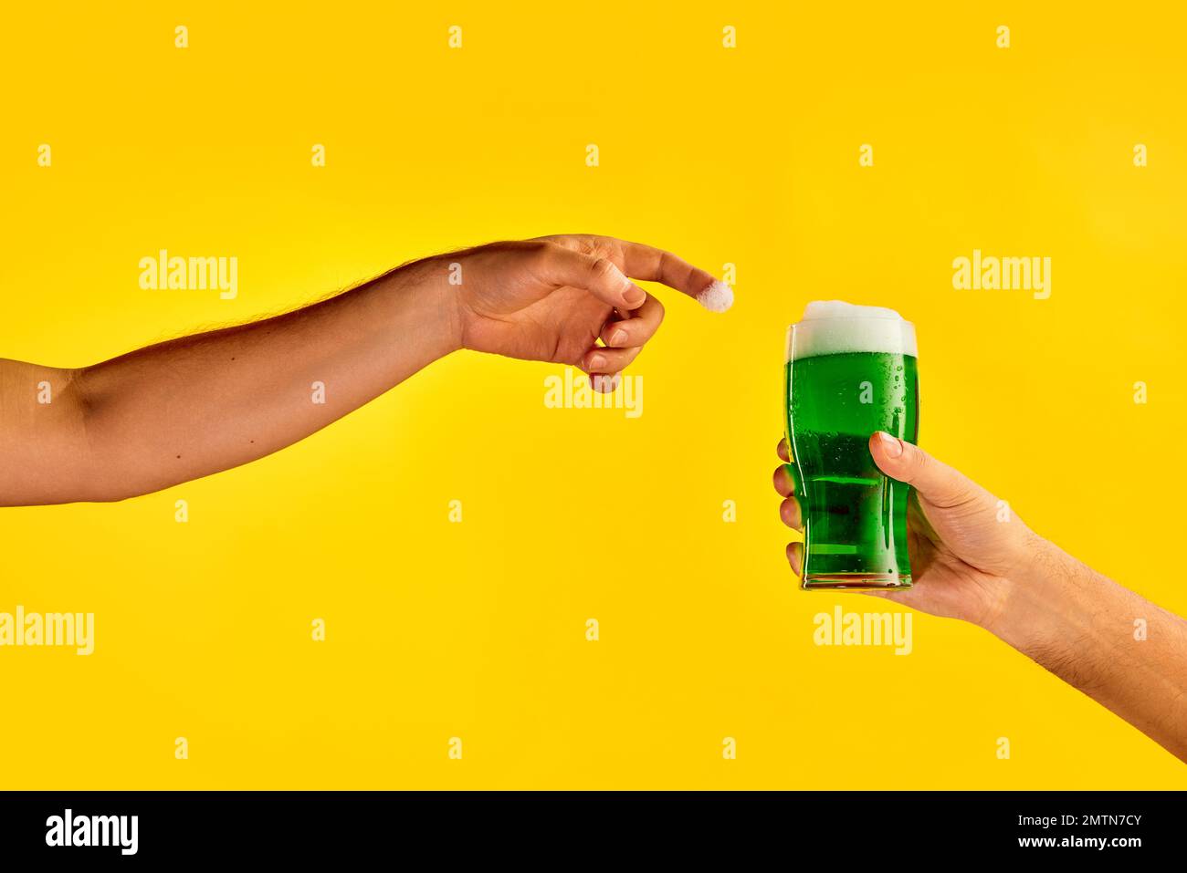 Male hand reaching glass with green foamy frothy beer over yellow ...
