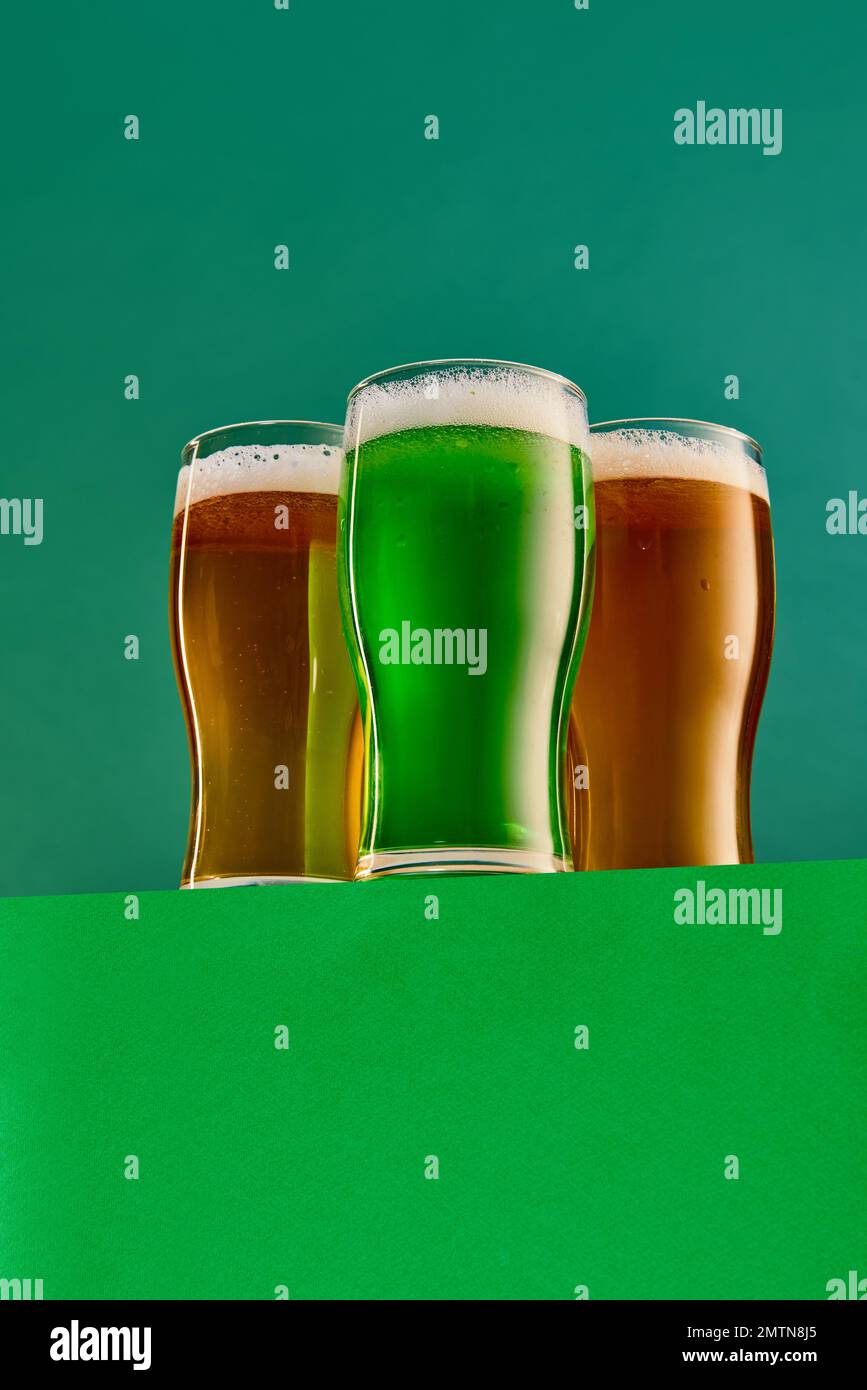 Three glasses with green and lager foamy beer over green background ...