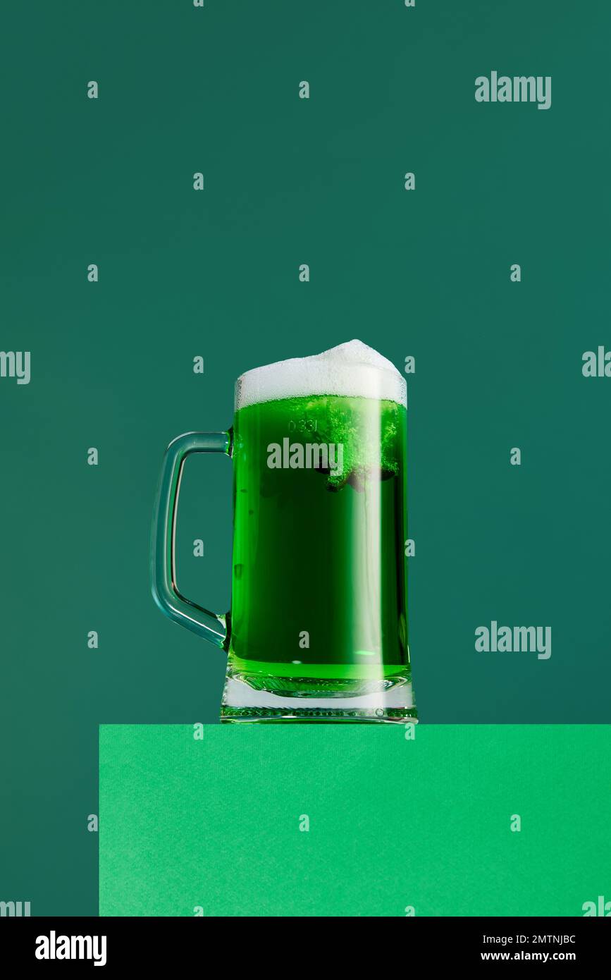 Anise taste. Mug with foamy green beer isolated over green background ...