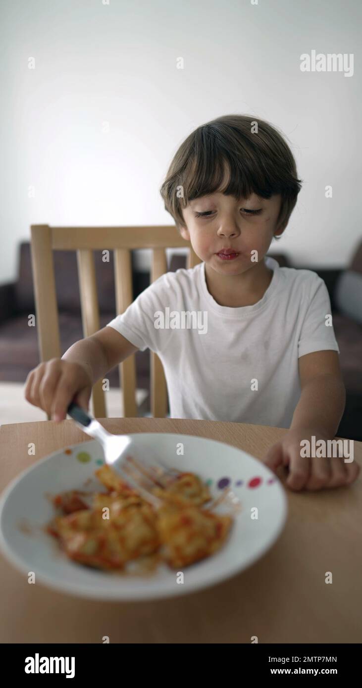 Small boy eating pasta on plate. Child eats lunch by himself. Carb food ...