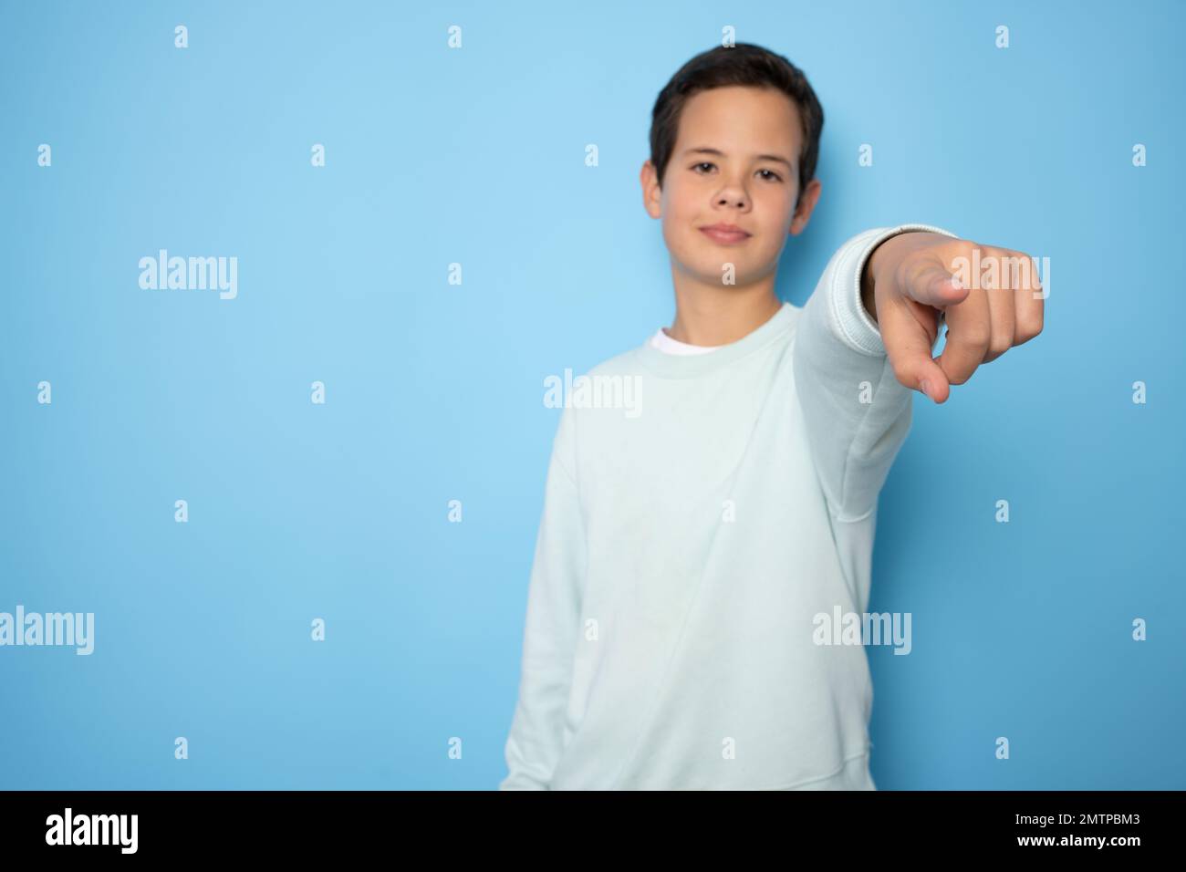 Boy looking and pointing to camera standing isolated over blue ...