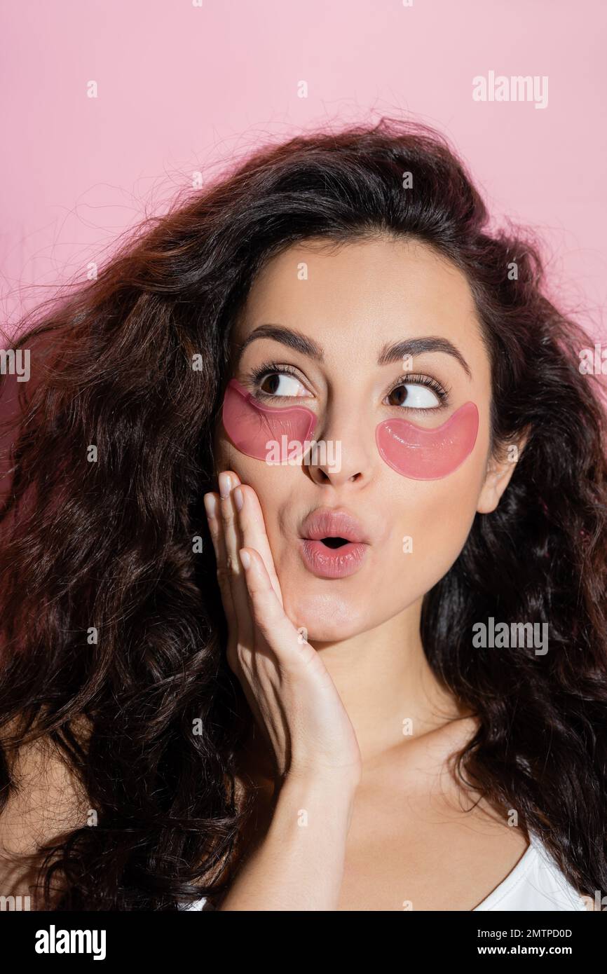 Dreamy woman with eye patches on face touching cheek on pink background ...
