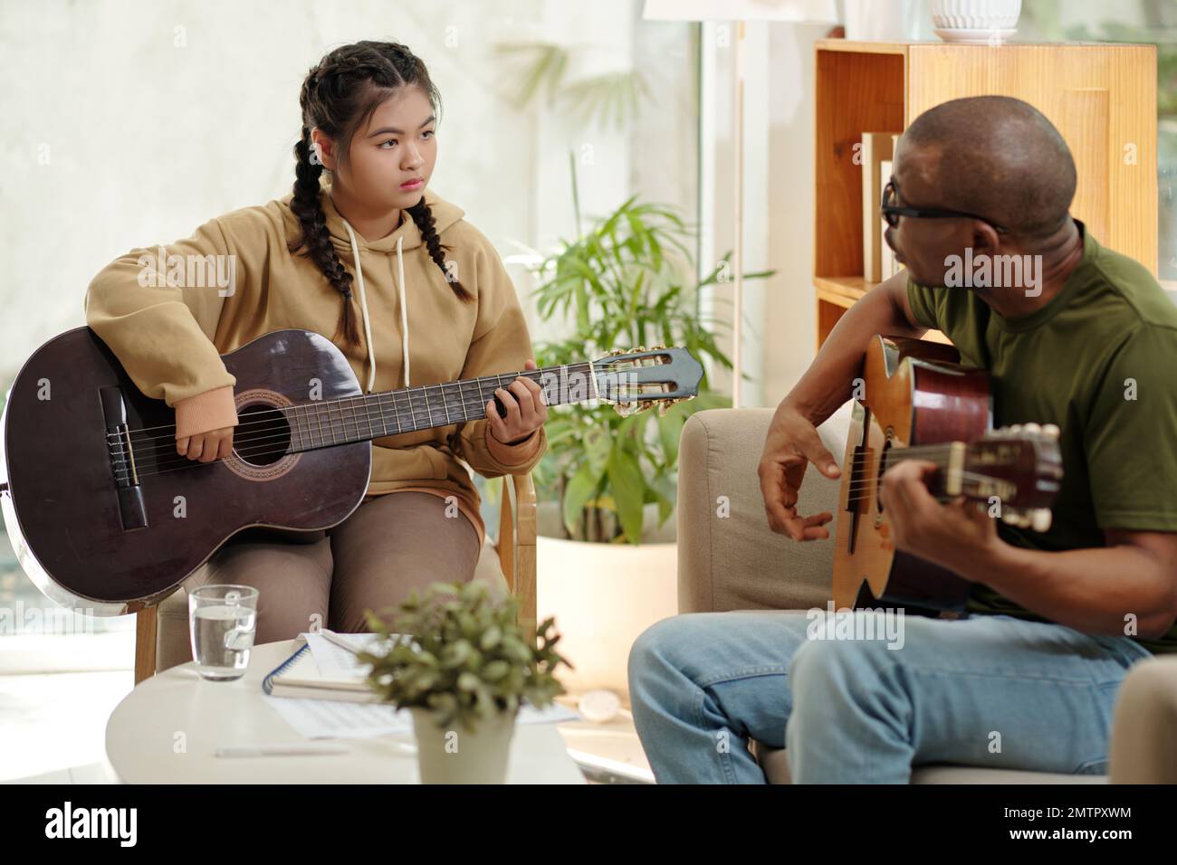 Confused teenage girl looking at teacher explaining how to play guitar ...