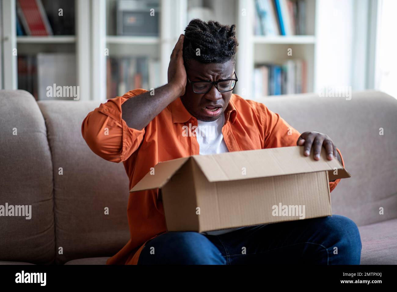 Disappointed african american young guy customer opening parcel box ...