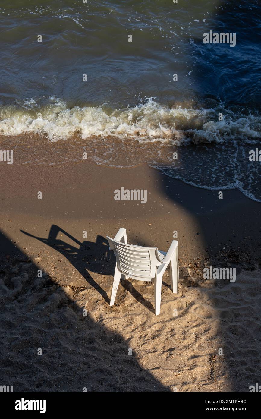 White plastic armchair on the wet beach in hot sunny time with shadow ...